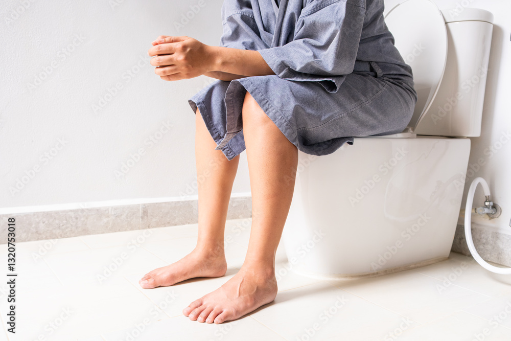 Woman sitting on the toilet bowl in the bathroom. She has stomach ache. Poor digestive system ...