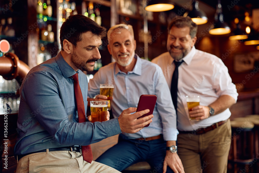 Smiling entrepreneur and his coworkers using cell phone while drinking ...