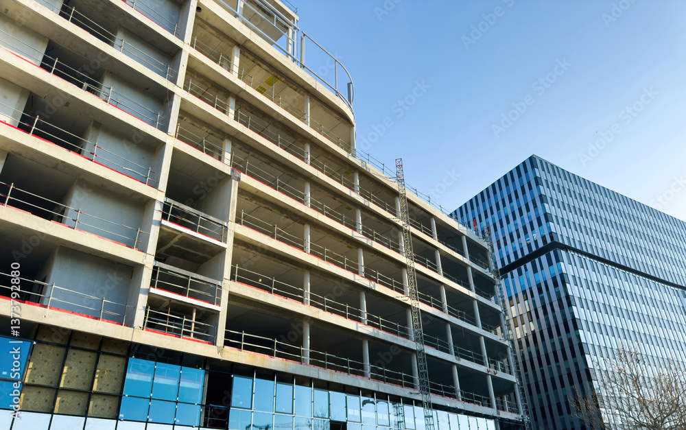 A multi-level concrete building under construction stands next to a ...