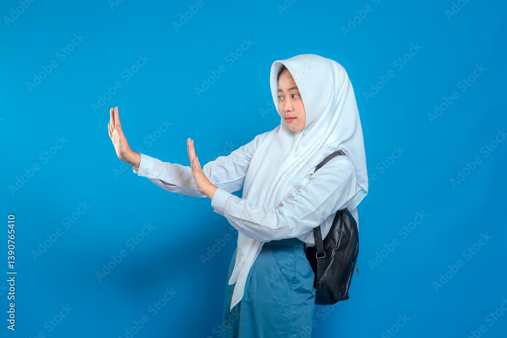 Serious-looking Muslim schoolgirl in uniform and hijab making a stop ...
