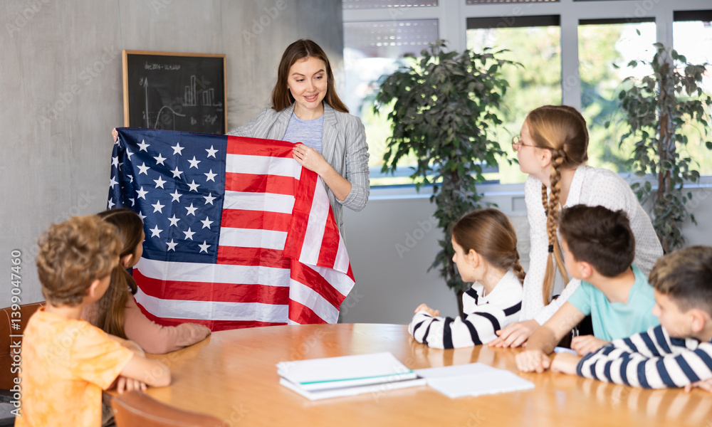 Smiling young woman teacher showing national flag of USA and telling ...