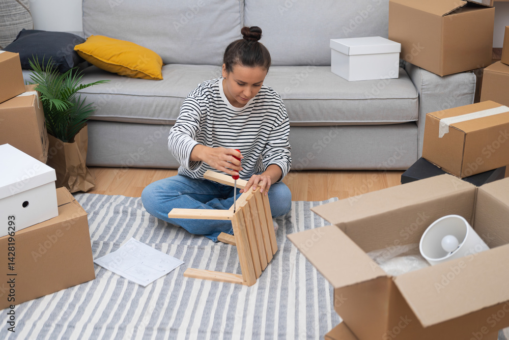 Tenant woman assembles shelf in her new house with screwdriver, amidst ...