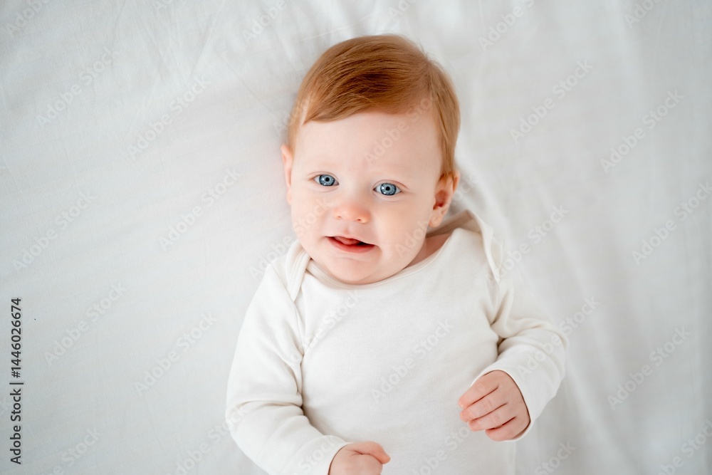 crying baby boy with red hair in a white bodysuit on the bed, top view ...