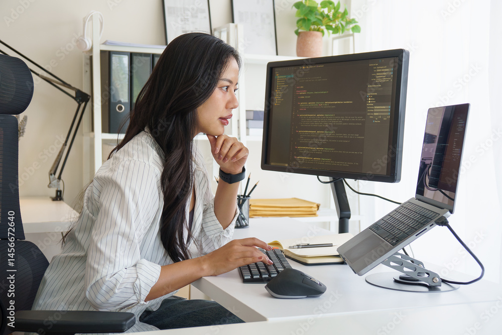Software developer working on coding project with multiple monitors in modern home office ...