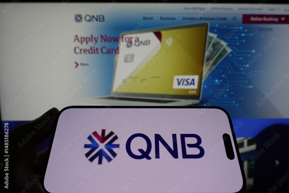 Kiel, Germany - 05-15-2025: Person holding smartphone with QNB logo on screen in front of the ...