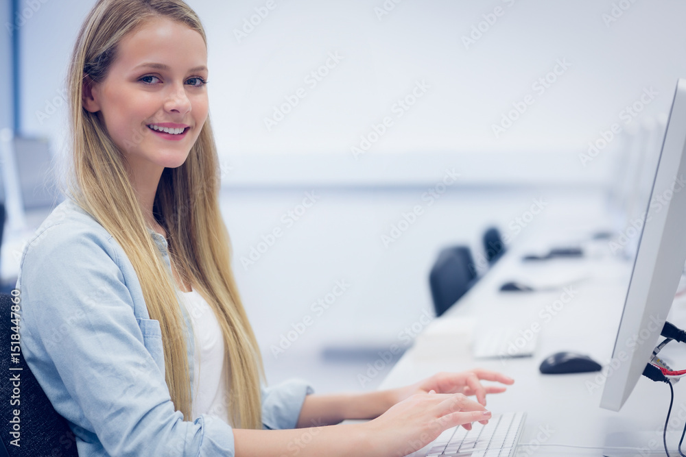Teenage girl smiling while typing at computer lab desk with keyboard ...