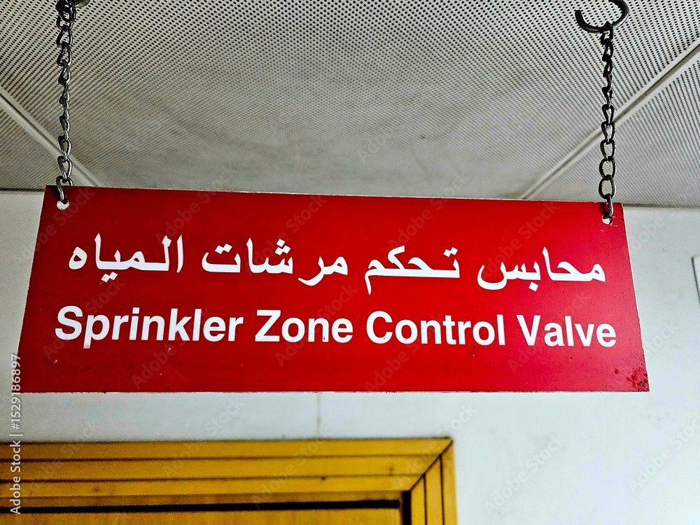 Red sign 'Sprinkler Zone Control Valve' in English & Arabic, hanging ...