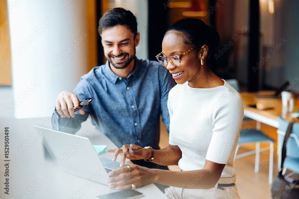 Two professionals at a desk using a laptop in a bright office setting ...