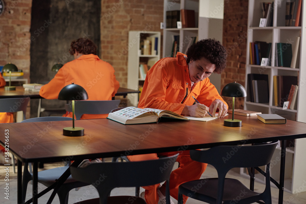 Young adult man wearing prison uniform sitting at table in prison ...