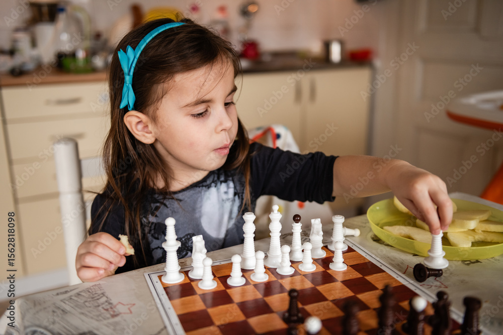 Little girl playing chess and eating apple slices at home Stock Photo ...