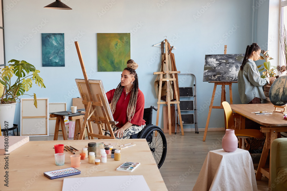 Young adult Caucasian woman with disability painting at easel in art ...