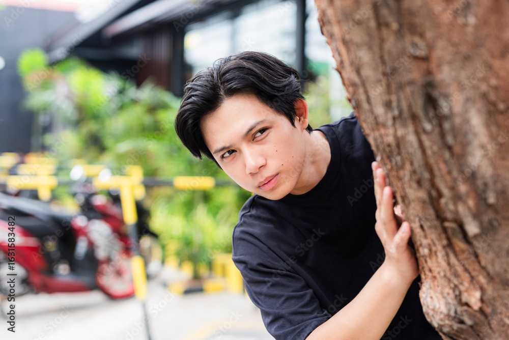 Sneaky young man hiding behind a tree while spying on ex-girlfriend and ...