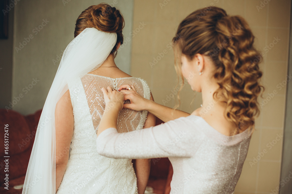Stock-Foto „Bridesmaid helping the bride fasten her lace wedding dress ...