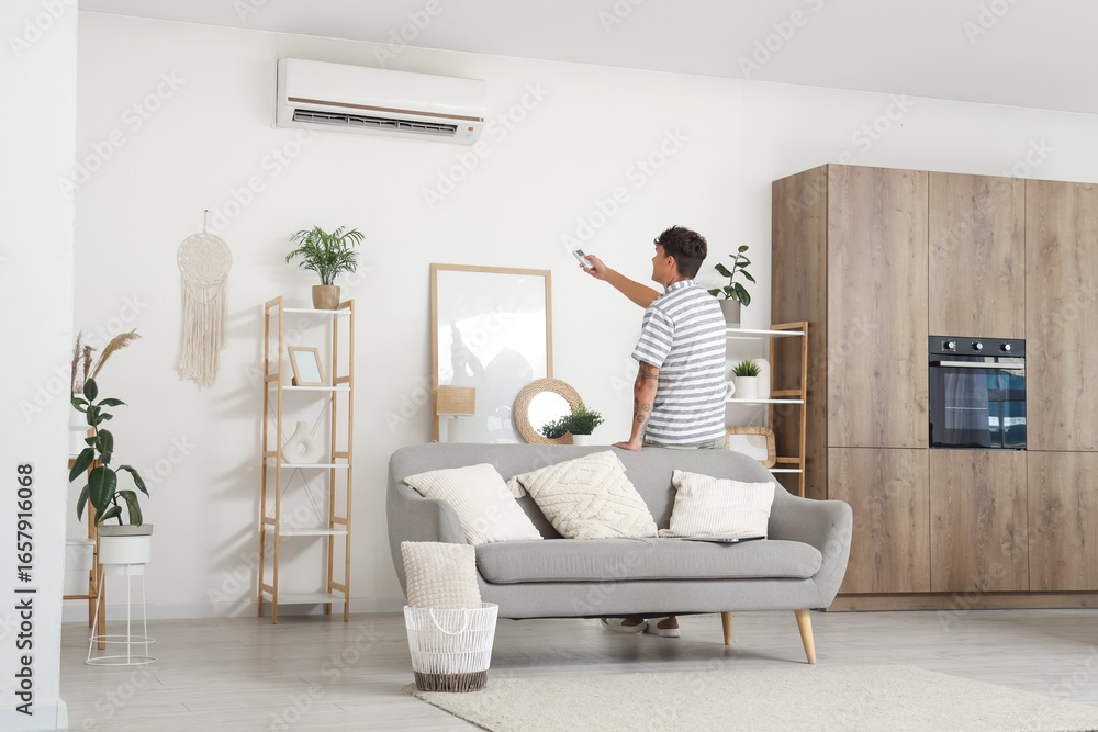 Handsome young man turning on air conditioner in living room, back view ...