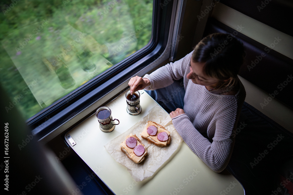 Стоковое фото «Woman on train eating sandwich, drinking tea while look ...