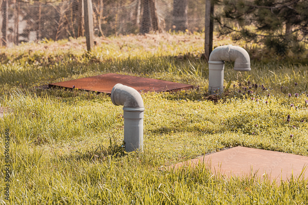 Septic tank system with ventilation pipes and metal covers on a grassy ...