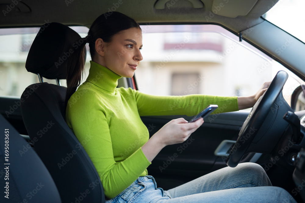 Careless young woman sitting behind the wheel of a car while holding a ...