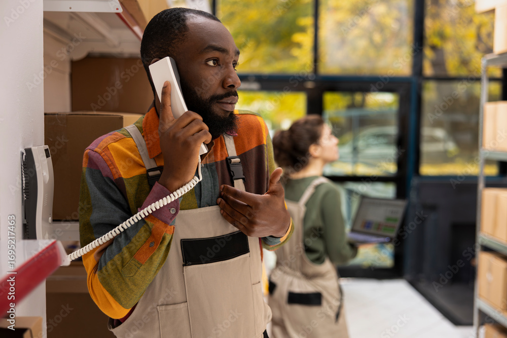Black male worker handling a landline phone call to check inventory ...