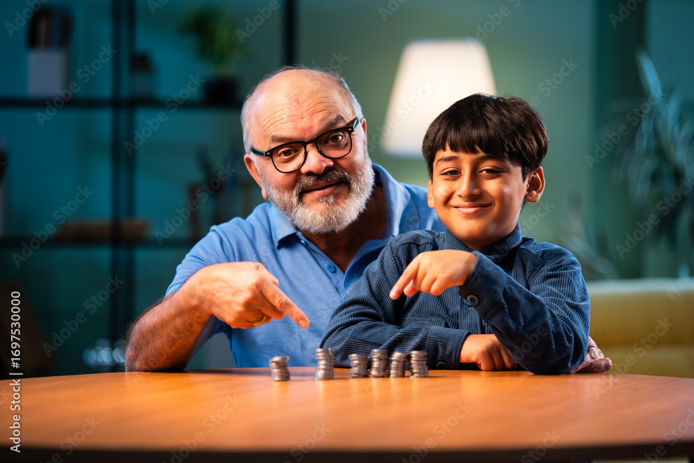 Indian grandfather and boy build coins tower at home, learning value of ...