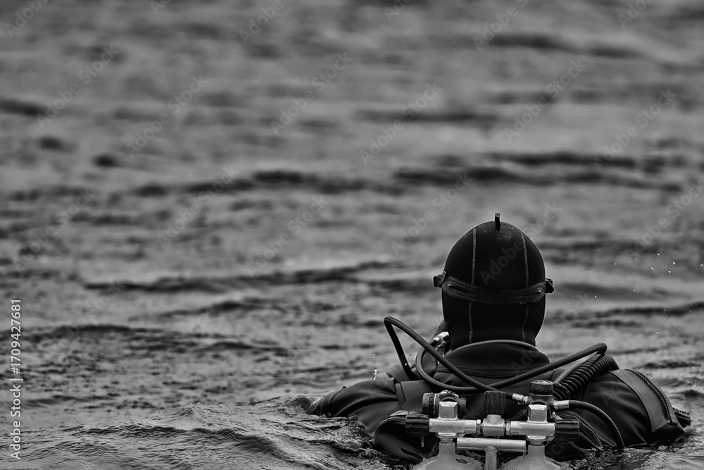 Diver in a dry suit prepares to dive into cold water, extreme diving ...