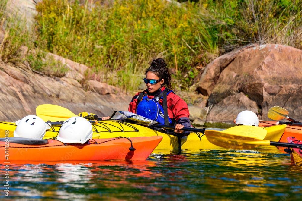 Outdoor adventure: a young woman checks the chart on her sea kayak deck ...