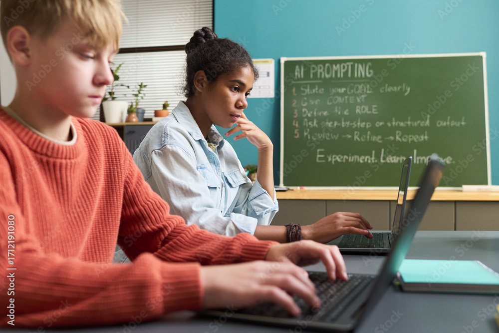 Teenage Caucasian boy and Black teenage girl working on laptops in ...