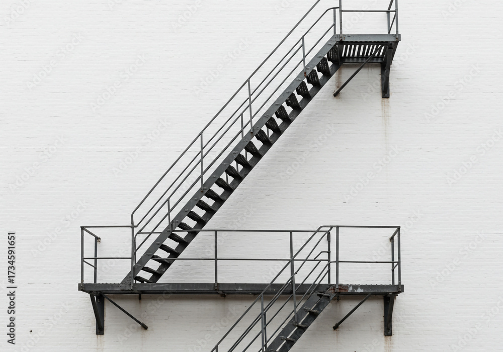 Modern metal fire escape ladders ascend a clean white brick wall ...