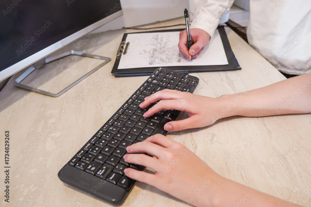 One person typing on a keyboard, while another takes notes in a folder ...