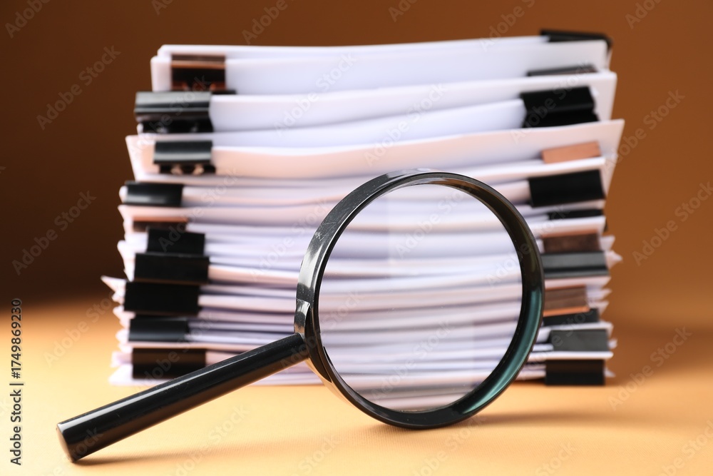 Magnifying glass and many documents with binder clips on brown ...