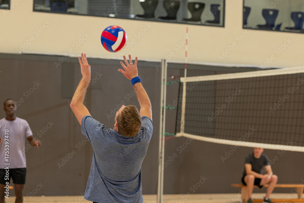 Diverse male teammates practicing volleyball in gymnasium with ...