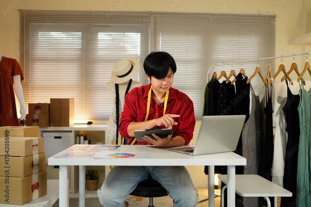 Male tailor work on items design with sketches, using laptop to review ...