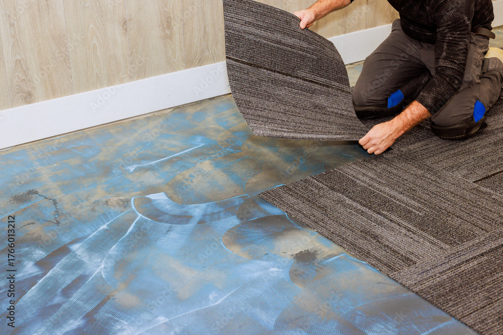 Contractor laying down new carpet tiles on living room floor, enhancing ...