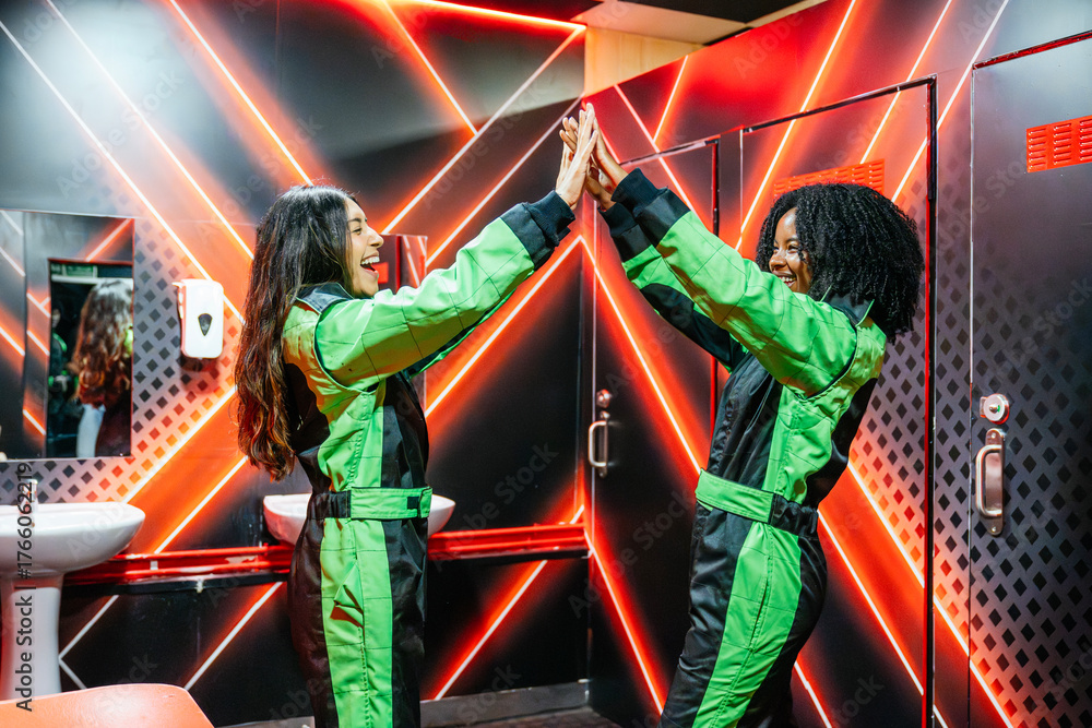 Two young women wearing green and black racing suits high fiving in a ...