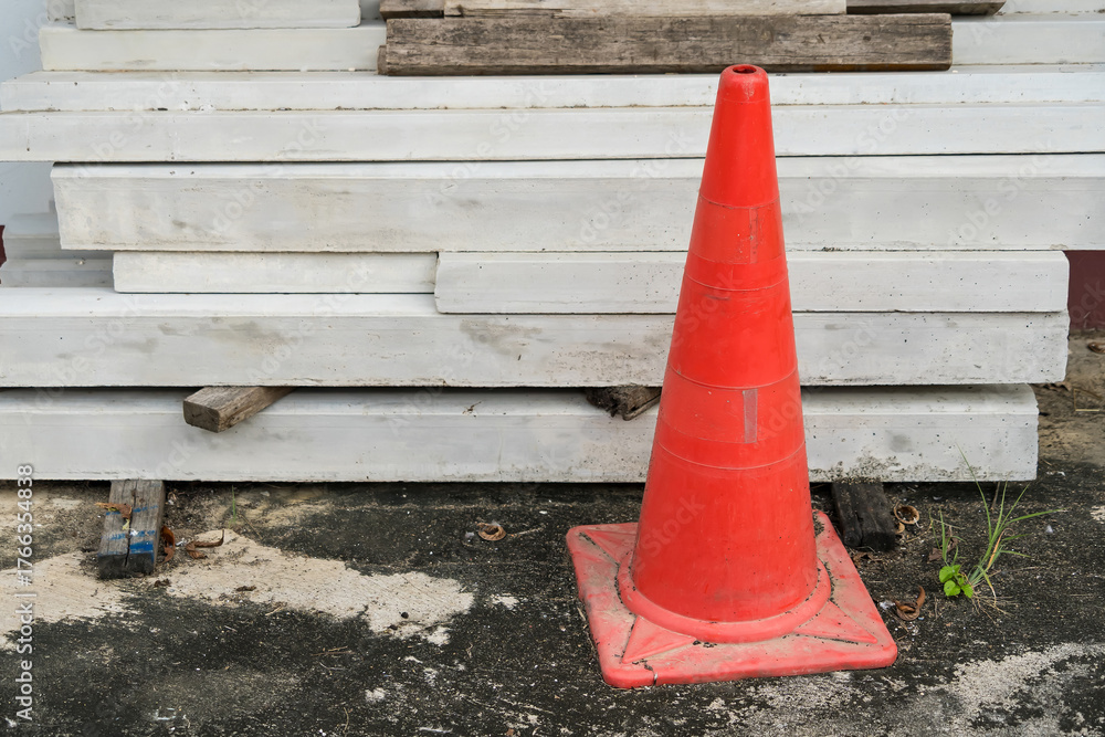 Bright orange traffic cone standing on worn asphalt in front of stacked ...
