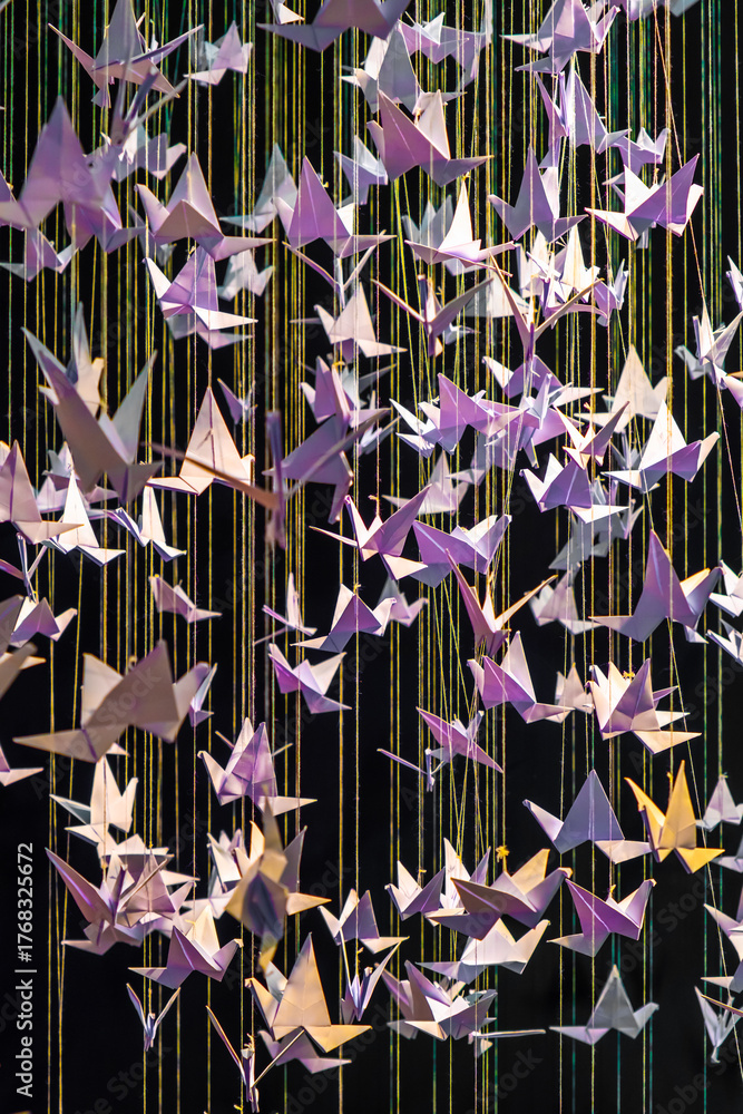 paper origami birds tied to strings hanging in air against a black ...