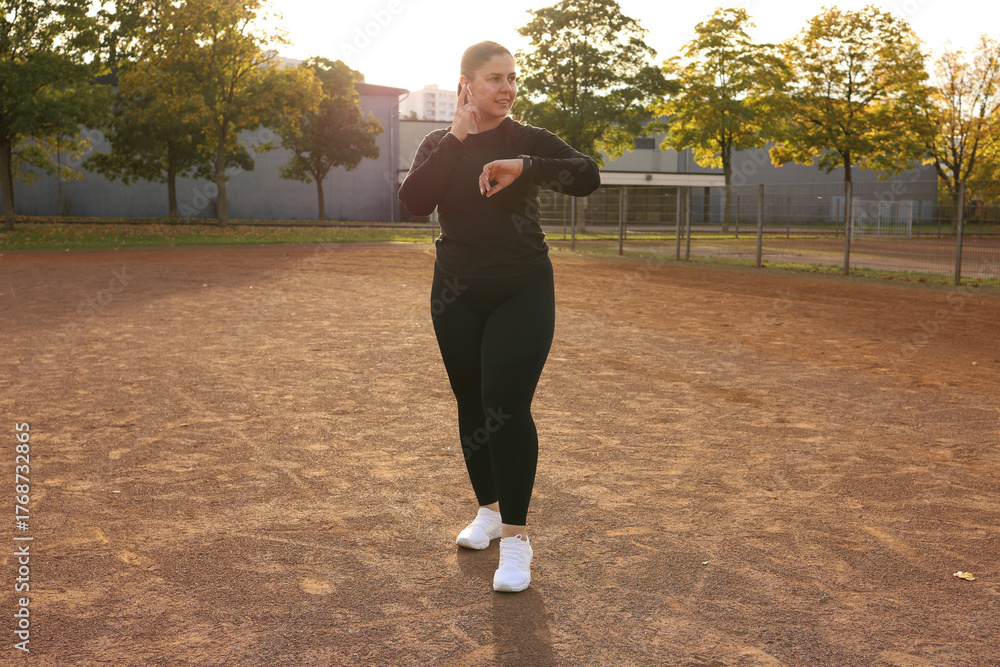 Beautiful overweight woman in sportswear doing squat exercise outdoors ...
