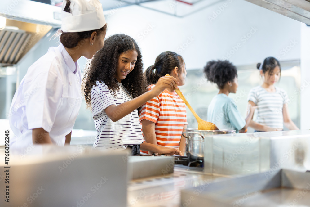 Professional female chef teaching diverse group of kids how to cook in ...