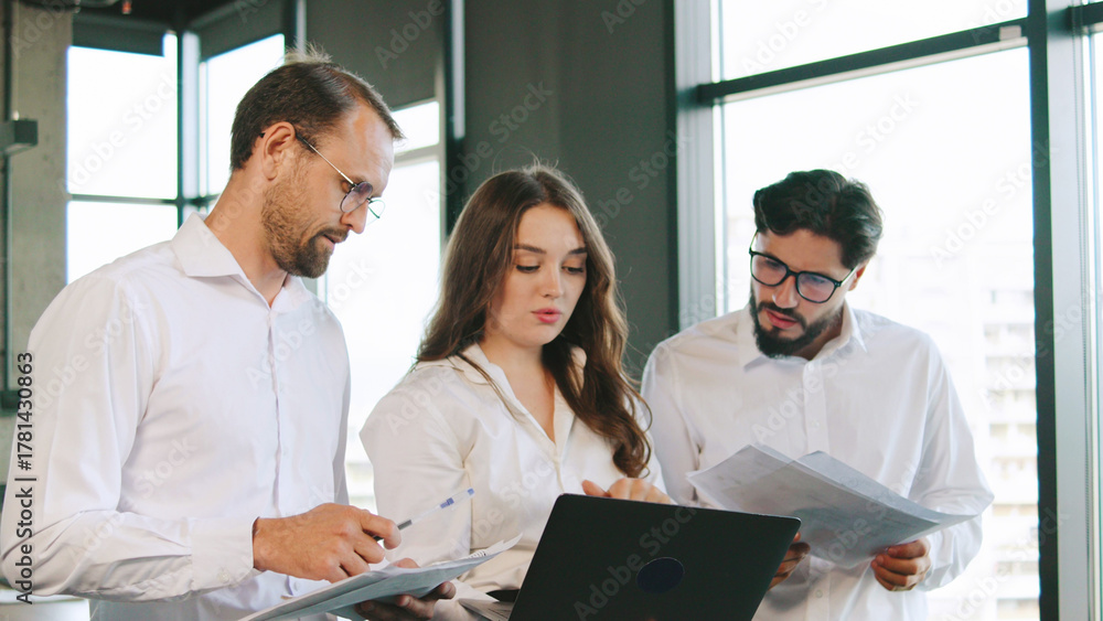 Three professionals review project documents and data on a laptop while ...