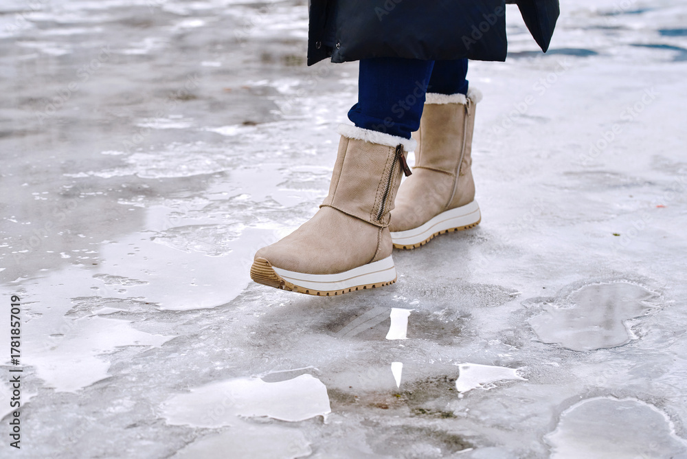 Suede boots stepping on icy frozen path with puddles during wet winter ...