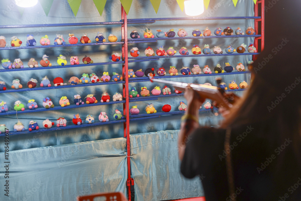 Focused woman has fun playing shooting gallery game at carnival. She ...