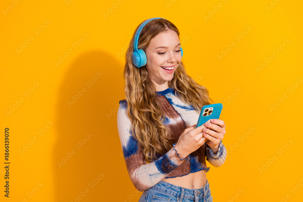 Young woman with blue headphones smiling at her phone against a bright ...