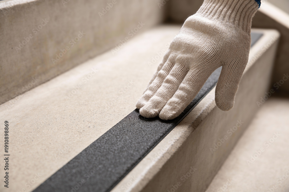 Gloved hand applying anti-slip tape to concrete stairs for safety and ...