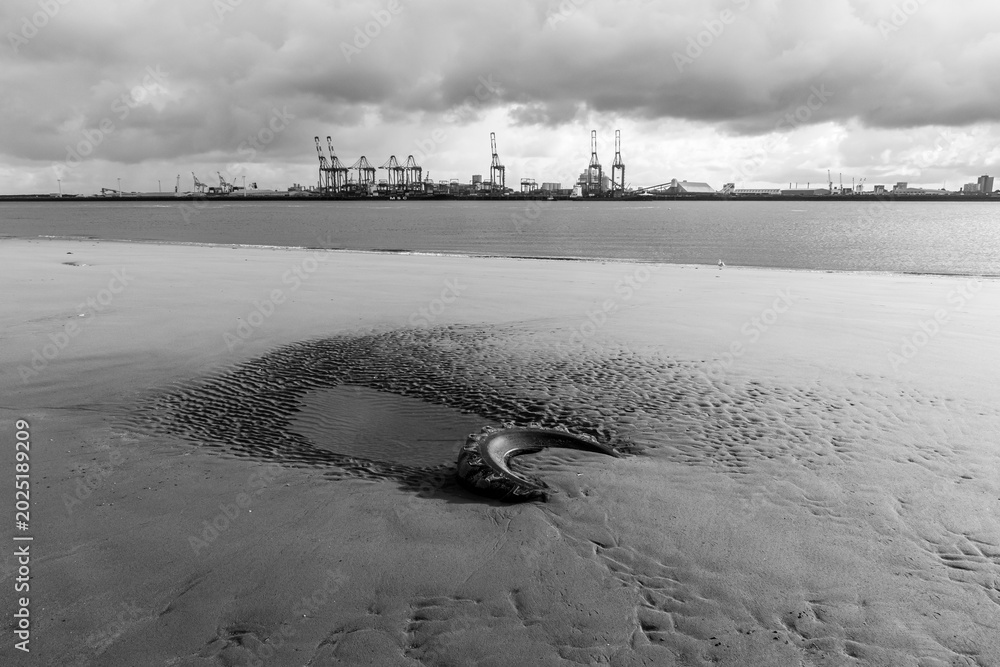 Monochrome view of a discarded tyre half-buried in sand at New Brighton ...