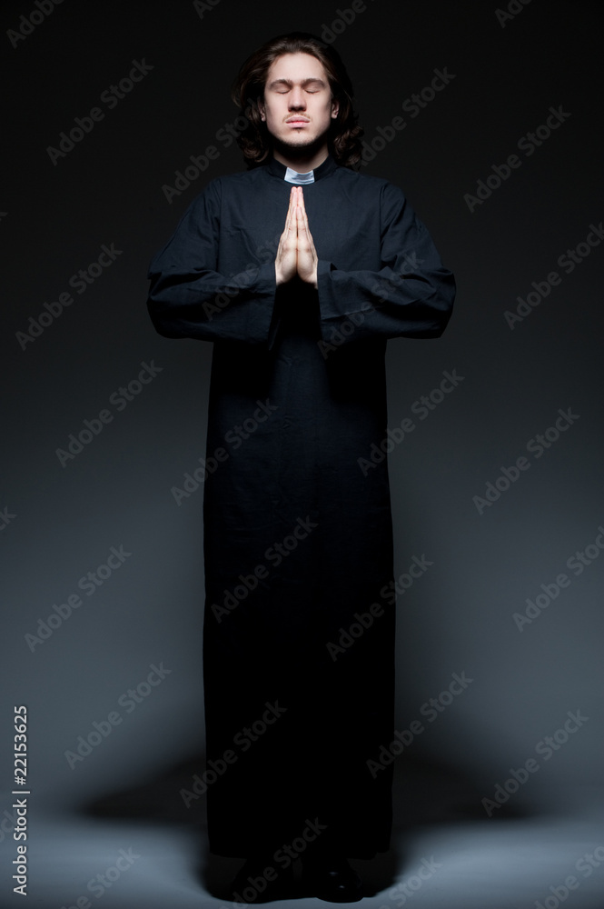 young priest is praying against dark background Stock Photo | Adobe Stock