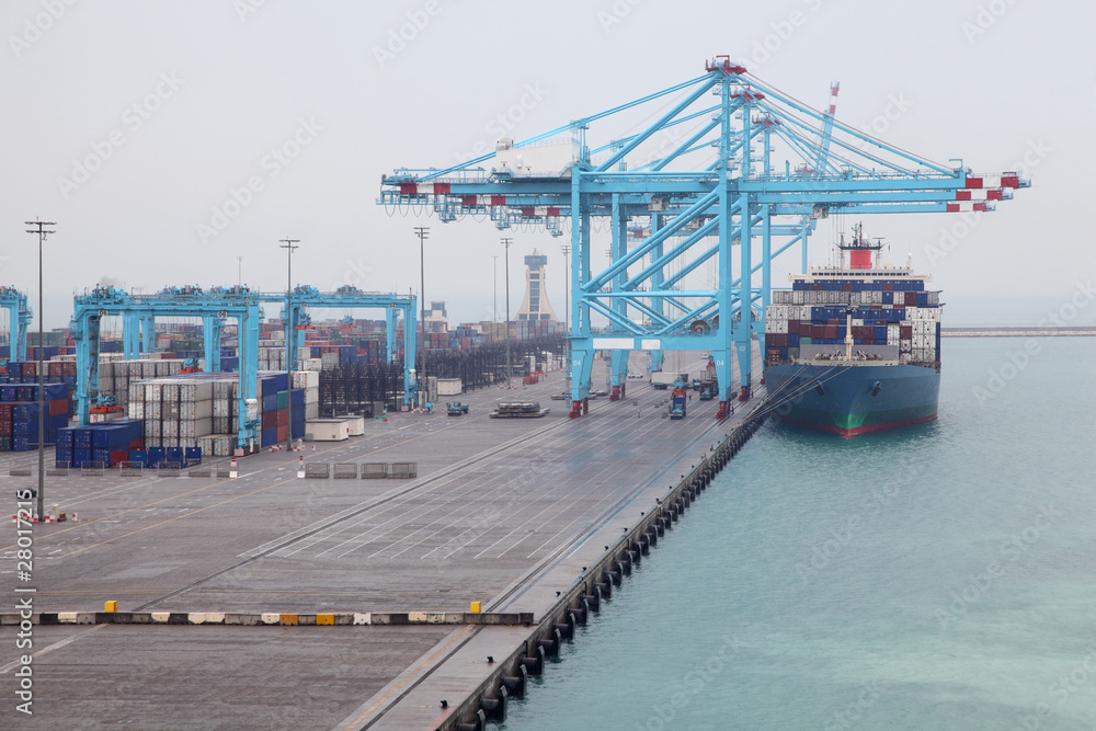Men load cargo boat docked to industrial port with blue cranes Stock ...