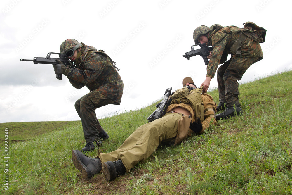 Soldiers saving their wounded colleague.Armed military men with guns ...