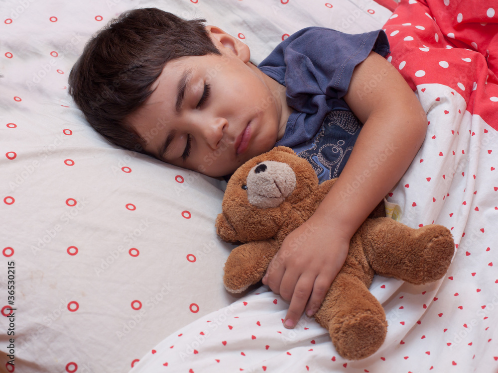 Foto Stock bambino che dorme nel letto con orsetto | Adobe Stock