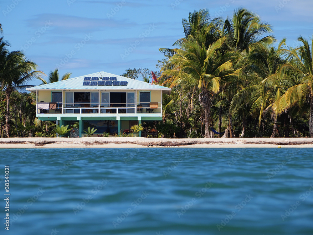 Beach house with solar panels on a tropical beach seen from water ...