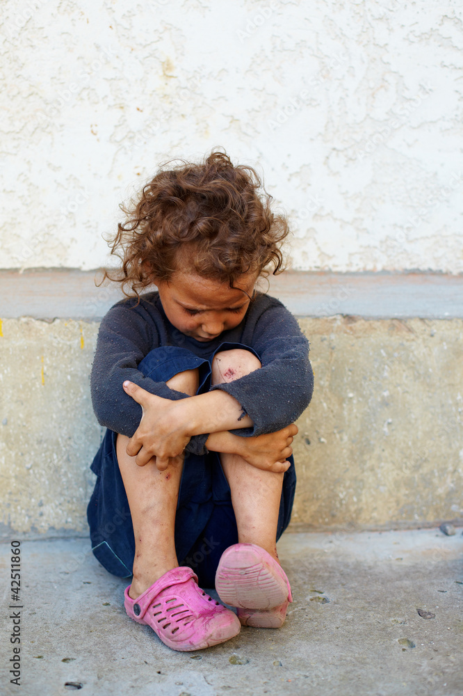 poor, sad little child girl sitting against the concrete wall Stock ...