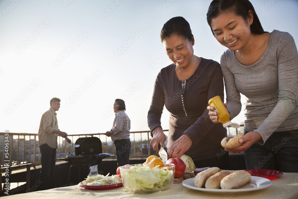 Mother and daughter preparing hot dogs for barbeque, father and son ...